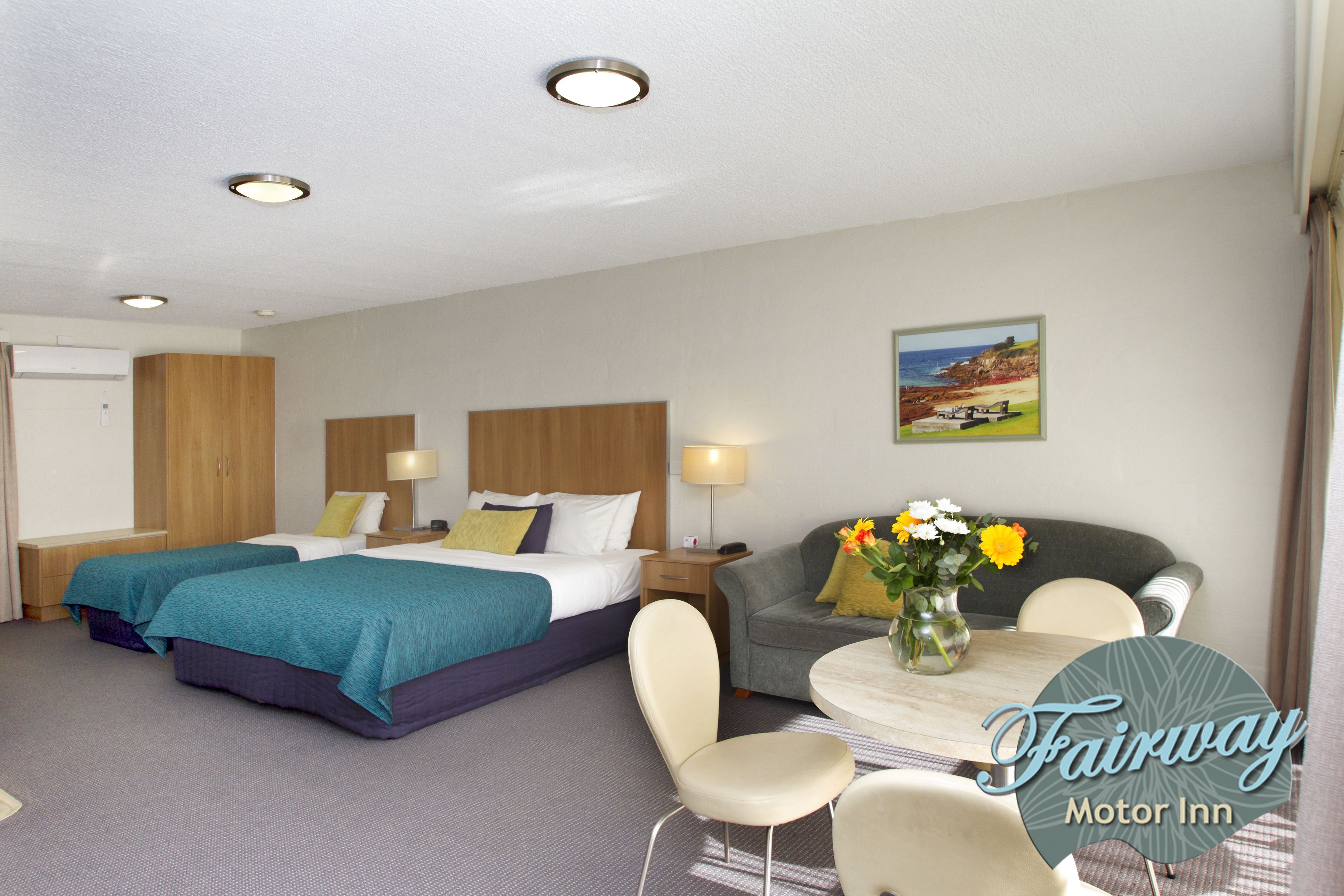 Quarto de hotel com duas camas, um sofá, uma cadeira, uma mesinha e um quadro na parede.