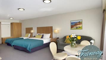 Quarto de hotel com duas camas, um sofá, uma cadeira, uma mesinha e um quadro na parede.