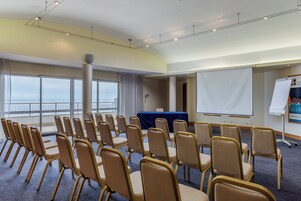 Uma sala de conferências com fileiras de cadeiras, uma tela de projetor e um quadro de apresentações.