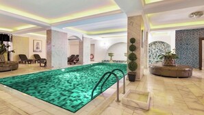Uma piscina interior espaçosa com chão em mosaico, rodeada por áreas de estar e design de interiores moderno.
