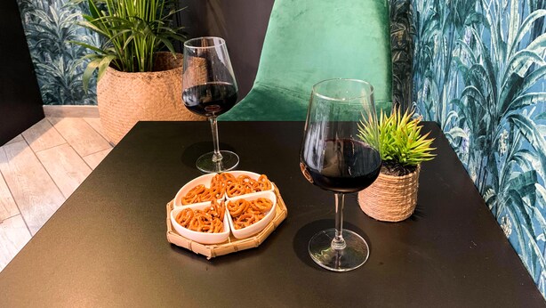 Uma mesa com duas taças de vinho e um prato de comida, cercada por plantas em vasos e uma cadeira.