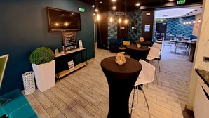 Interior moderno de restaurante com piso de madeira, mesas pretas e área de estar com sofá e cadeiras.