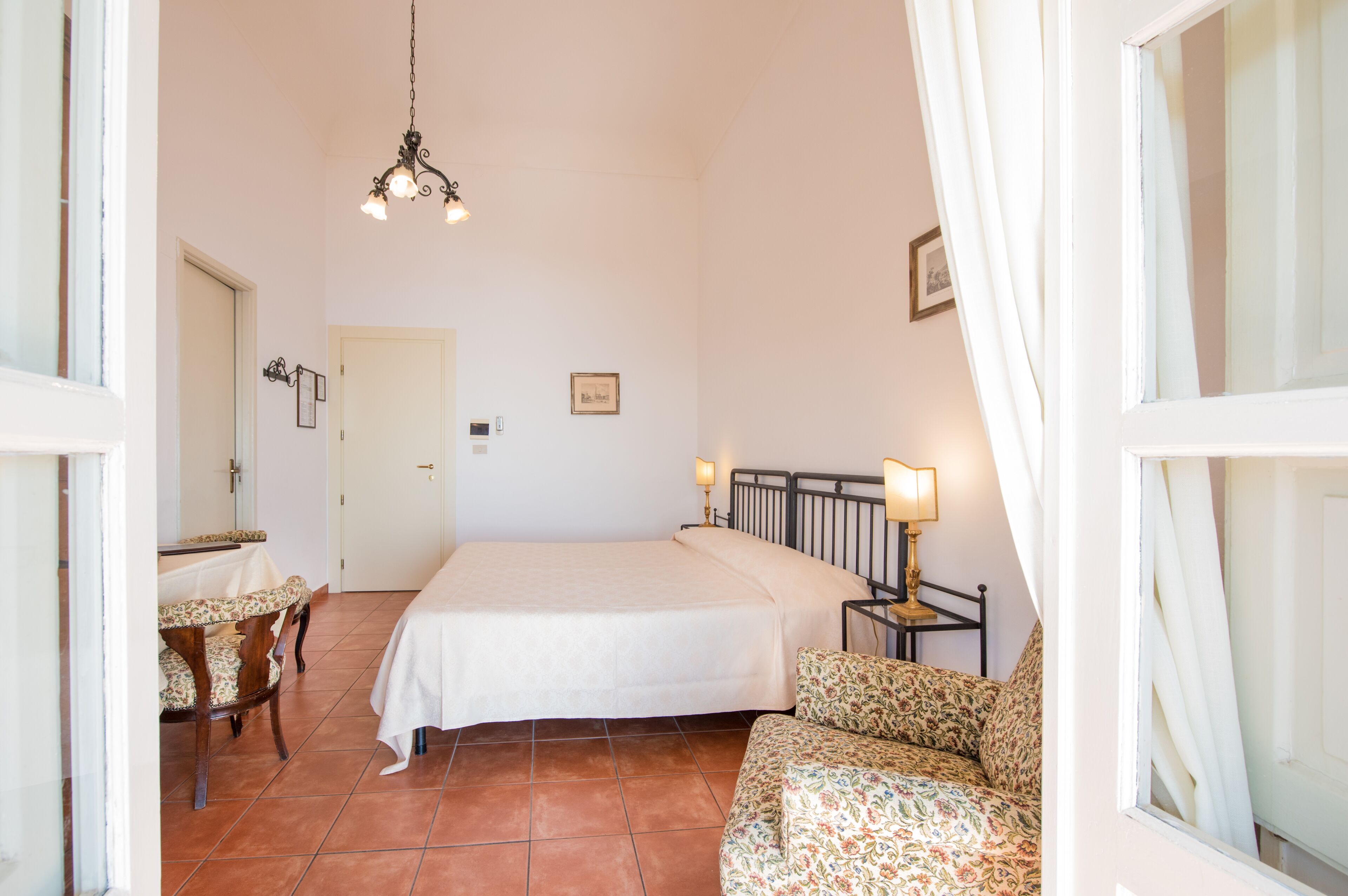 Quarto com cama, poltrona, mesa e luminária suspensa.