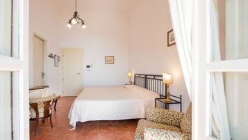 Quarto com cama, poltrona, mesa e luminária suspensa.