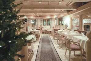 Um restaurante acolhedor com interiores em madeira, mesas preparadas para refeições e um pinheiro de Natal em primeiro plano.