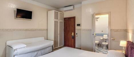 Quarto de hotel com uma cama, um sofá, uma televisão, ar condicionado e um banheiro visível por uma porta aberta.