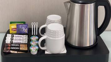 Uma bandeja com uma cafeteira, duas xícaras brancas, talheres e alguns alimentos, incluindo chá Lipton e café Nescafé.