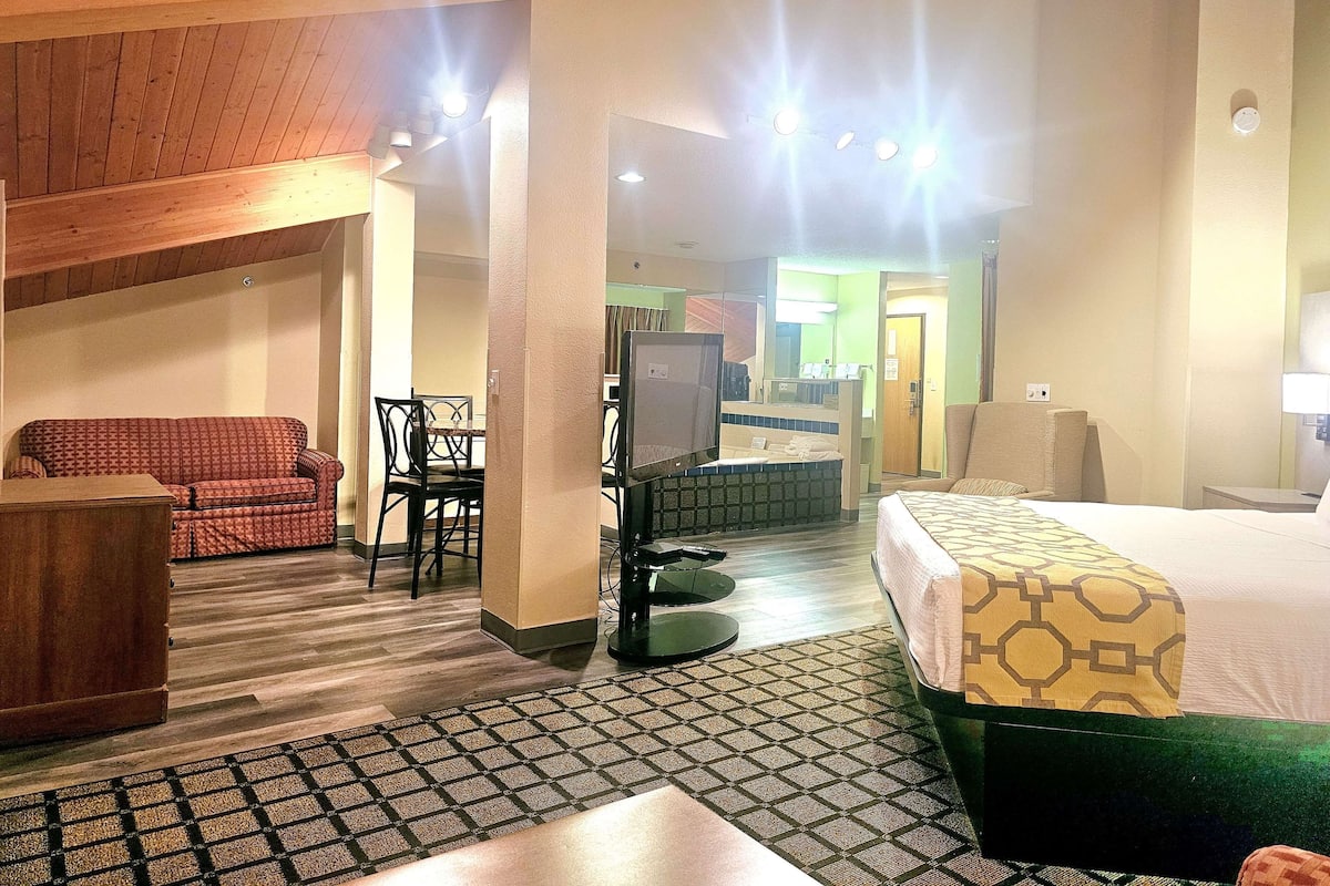Quarto de hotel com cama, sofá, escrivaninha e televisão.