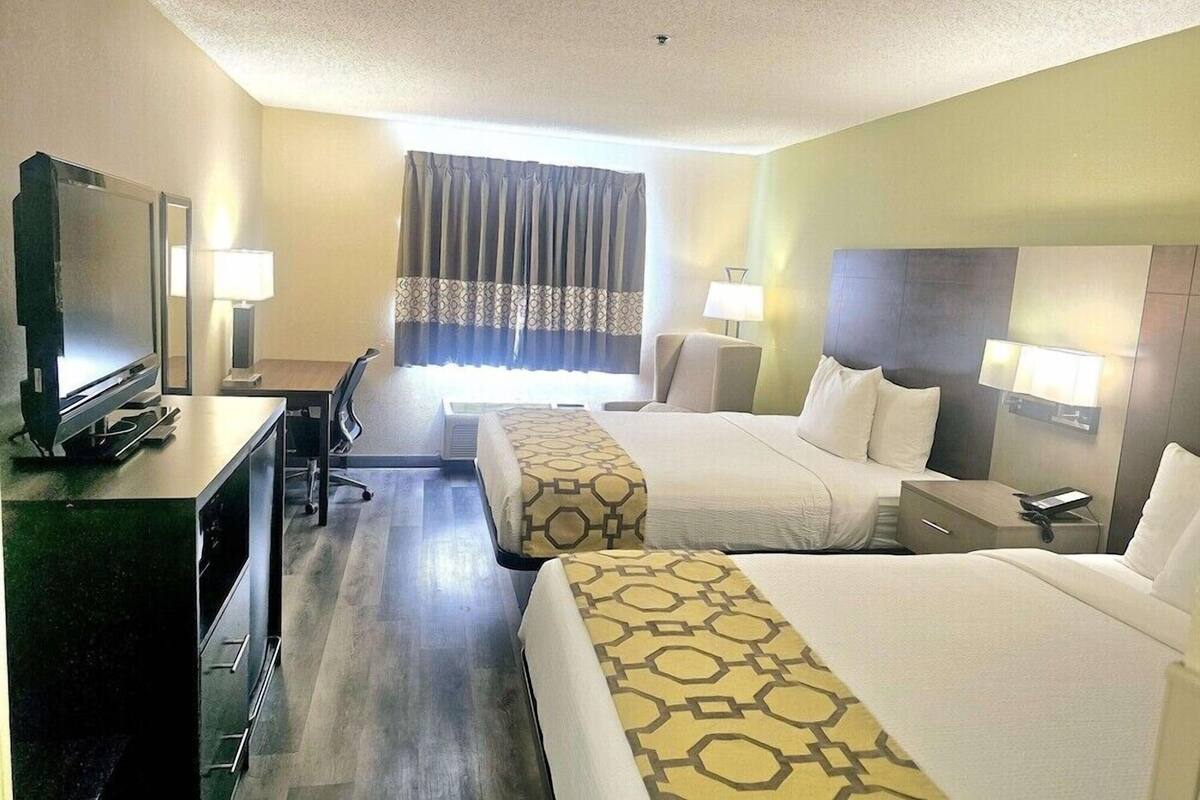 Quarto de hotel com duas camas, uma escrivaninha, televisão e janela com cortinas.