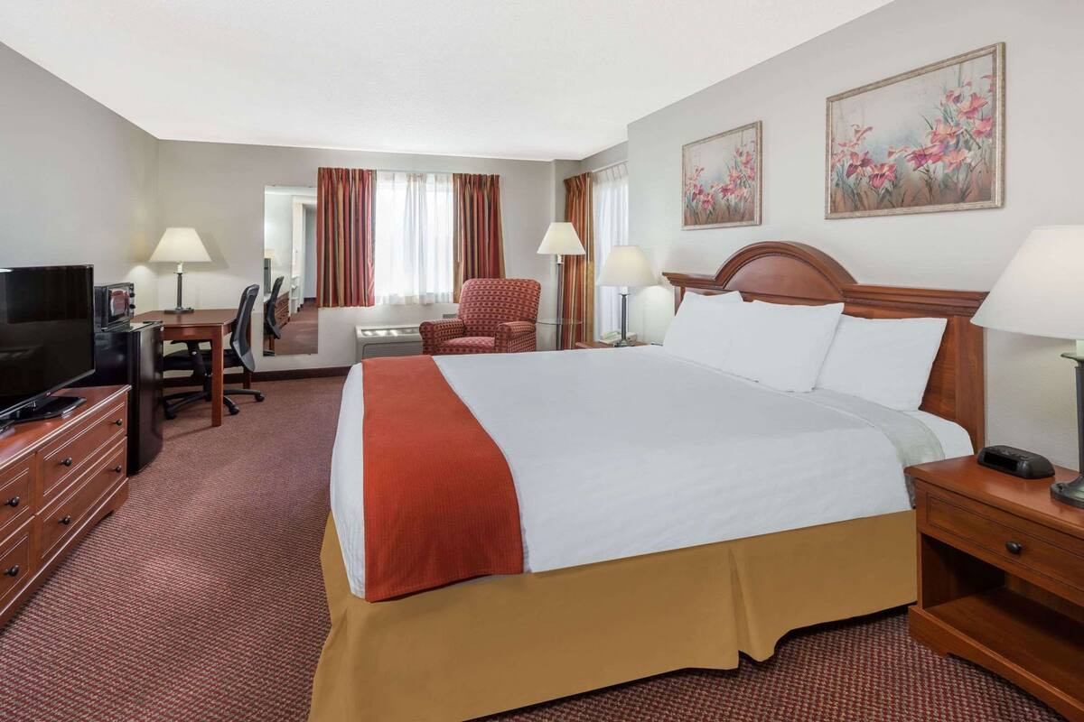 Quarto de hotel com cama, escrivaninha, televisão, cadeira e obras de arte nas paredes.