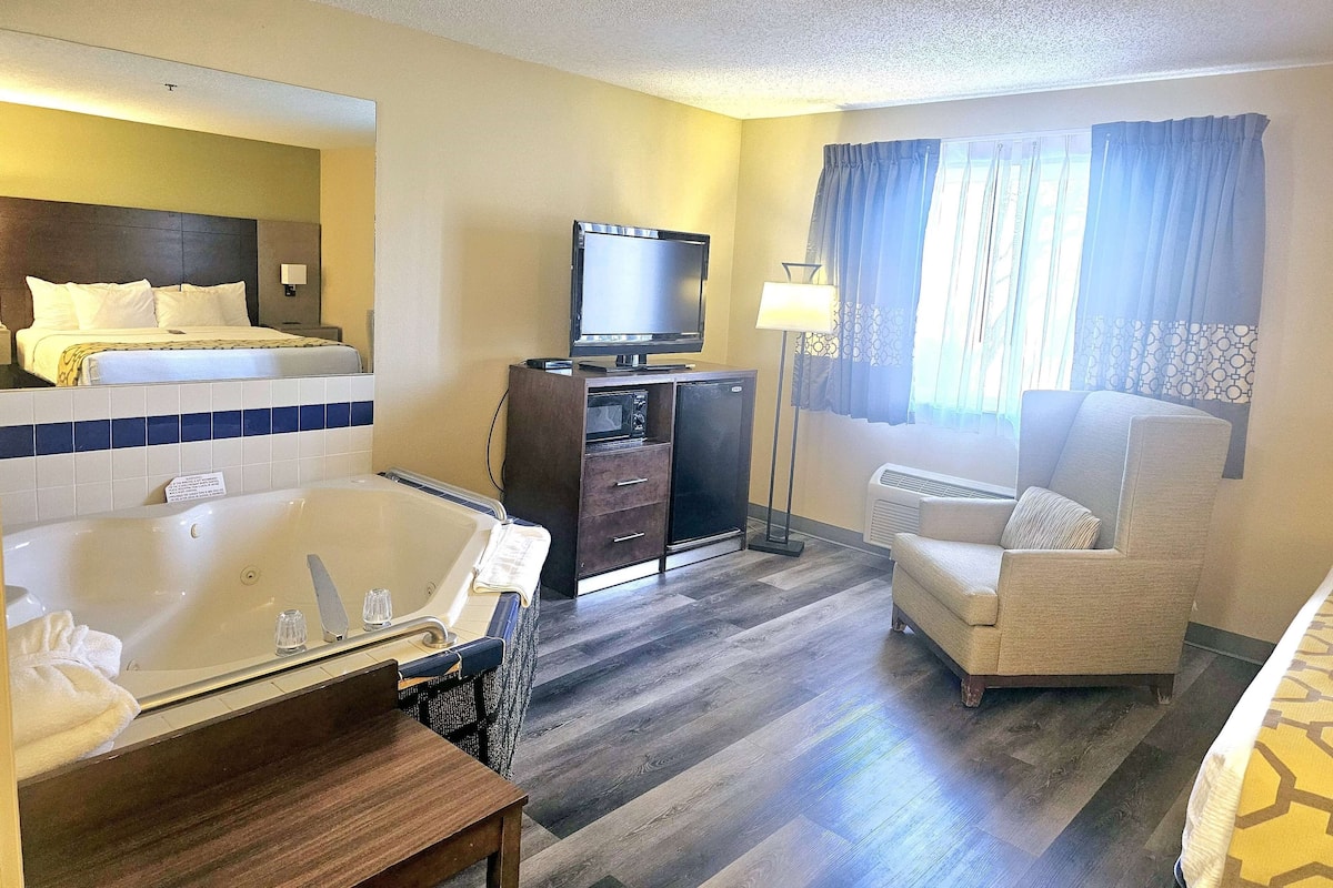 Quarto de hotel com uma banheira grande, televisão, sofá e escrivaninha com cadeira.