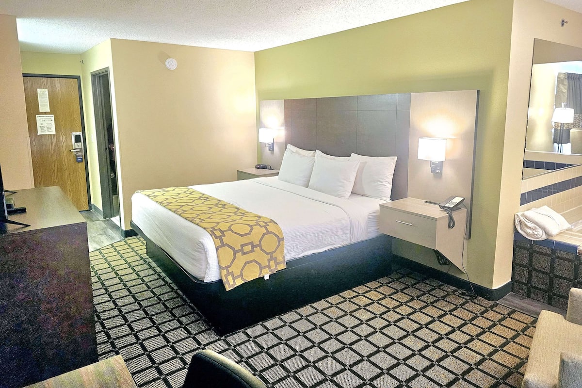 Quarto de hotel com cama, mesa de cabeceira, luminária e espelho.