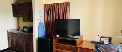 Quarto compacto com cozinha compacta, televisão de tela plana, escrivaninha, cadeira e geladeira.