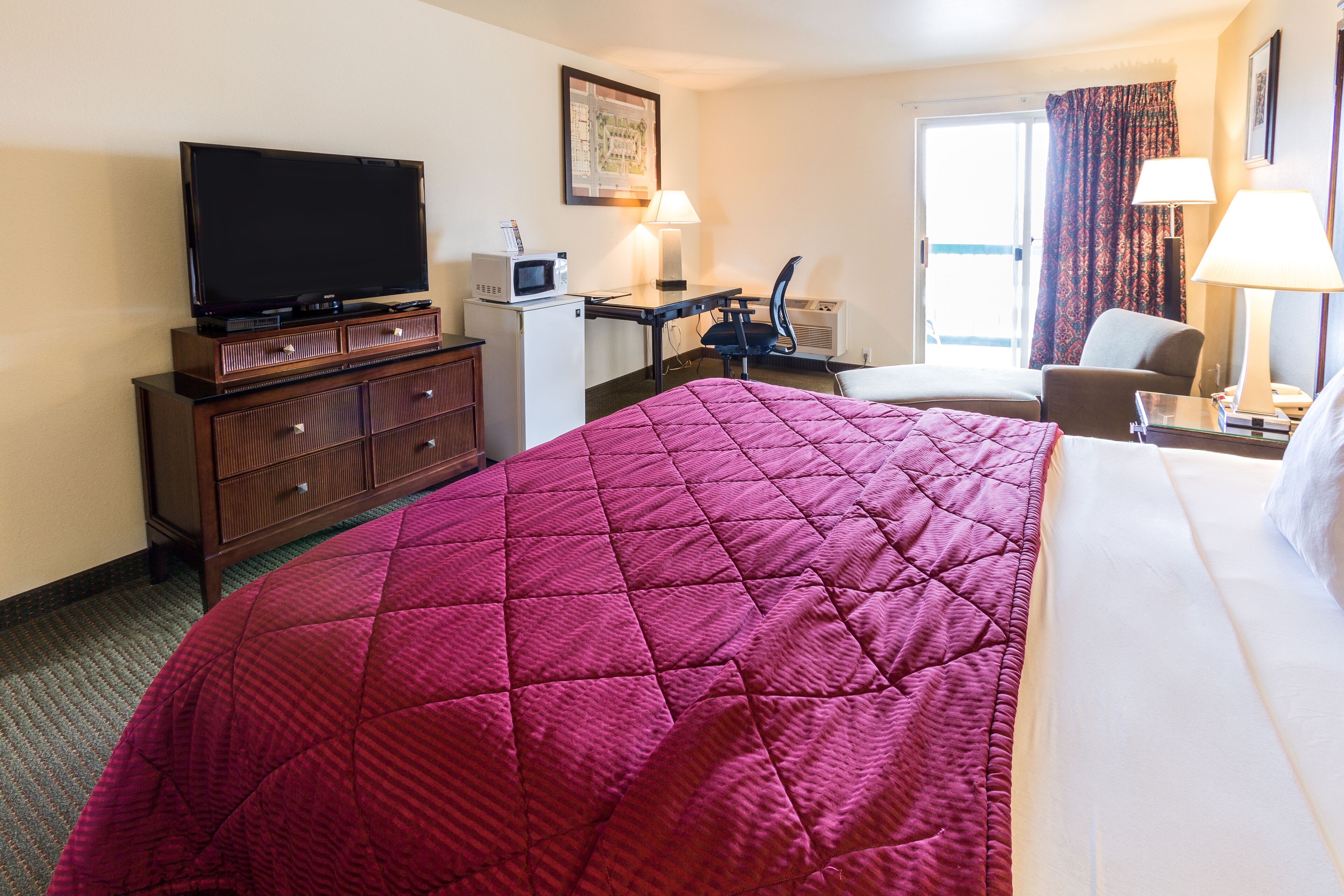 Quarto de hotel com uma cama grande, uma escrivaninha com computador, televisão e micro-ondas.