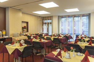 Uma sala de conferências com várias mesas preparadas para refeições, equipada com cadeiras, toalhas de mesa e louças.
