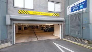 Entrada de um estacionamento com placa de altura máxima, sinalização de Holiday Inn Express e Ibis Hotel, e placa indicando estacionamento seguro.
