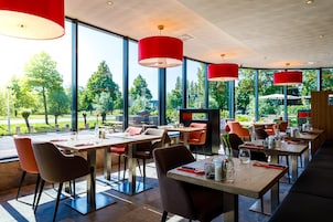Um restaurante moderno com janelas amplas, luminárias pendentes vermelhas e vista para o verde lá fora.