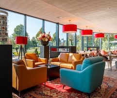 Uma área de estar moderna com assentos laranja e azuis, um abajur vermelho e uma grande janela com vista para a cidade.