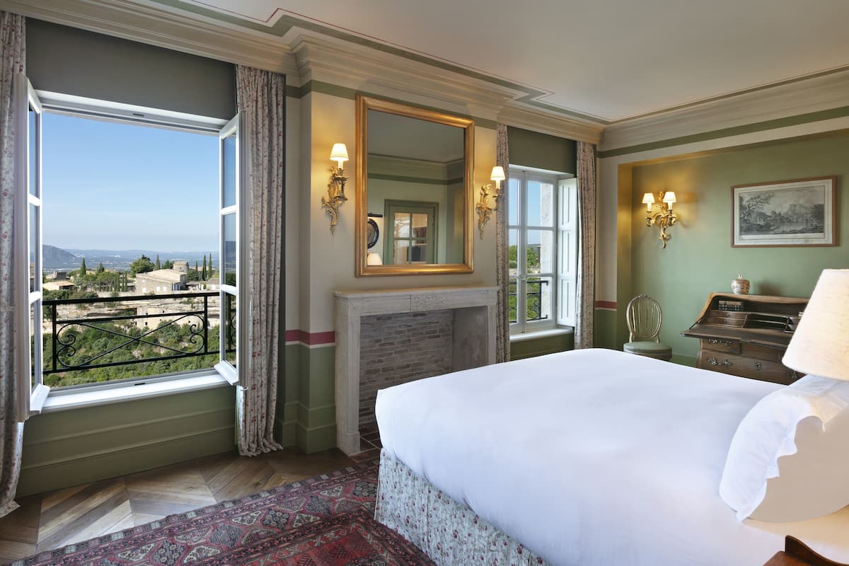 Quarto de hotel com uma cama grande, lareira, vista pela janela e um candelabro.