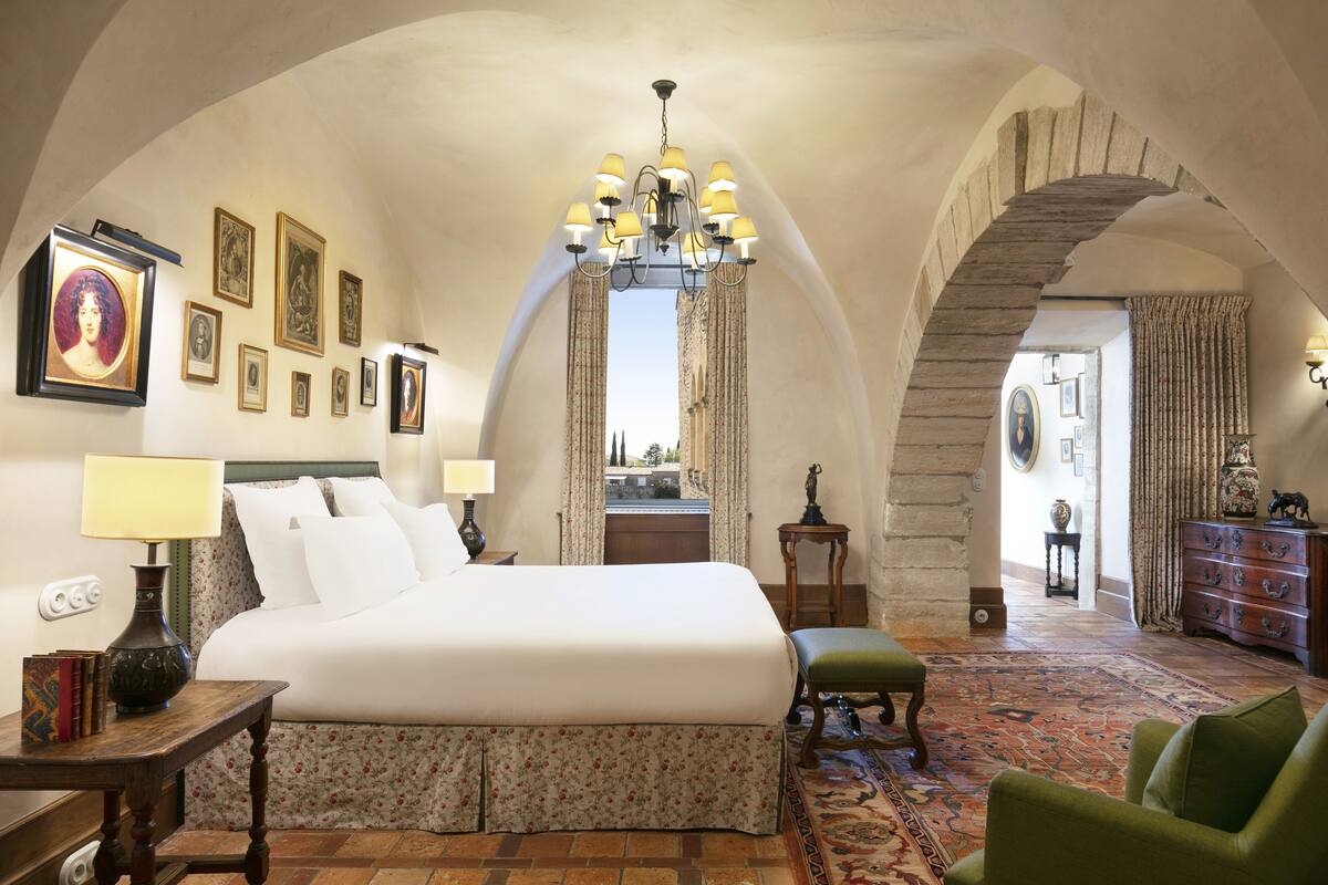 Quarto espaçoso com uma cama grande, um candelabro e vista através de uma porta arqueada.