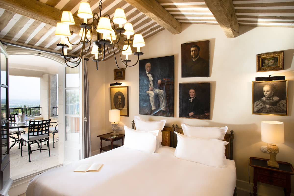 Quarto de hotel com uma cama grande, um candelabro e quadros nas paredes.