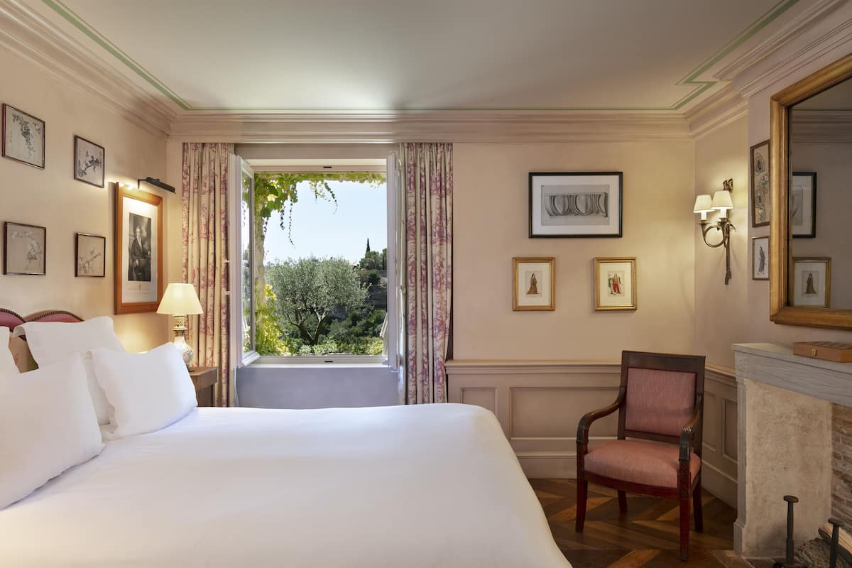 Quarto de hotel com uma cama grande, uma poltrona, lareira e quadros nas paredes.
