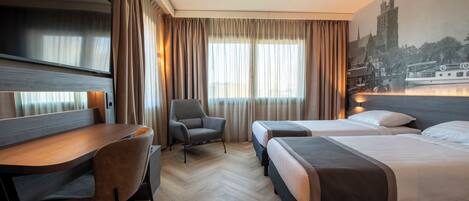 Quarto de hotel com escrivaninha, duas camas, uma cadeira e uma janela grande com cortinas.