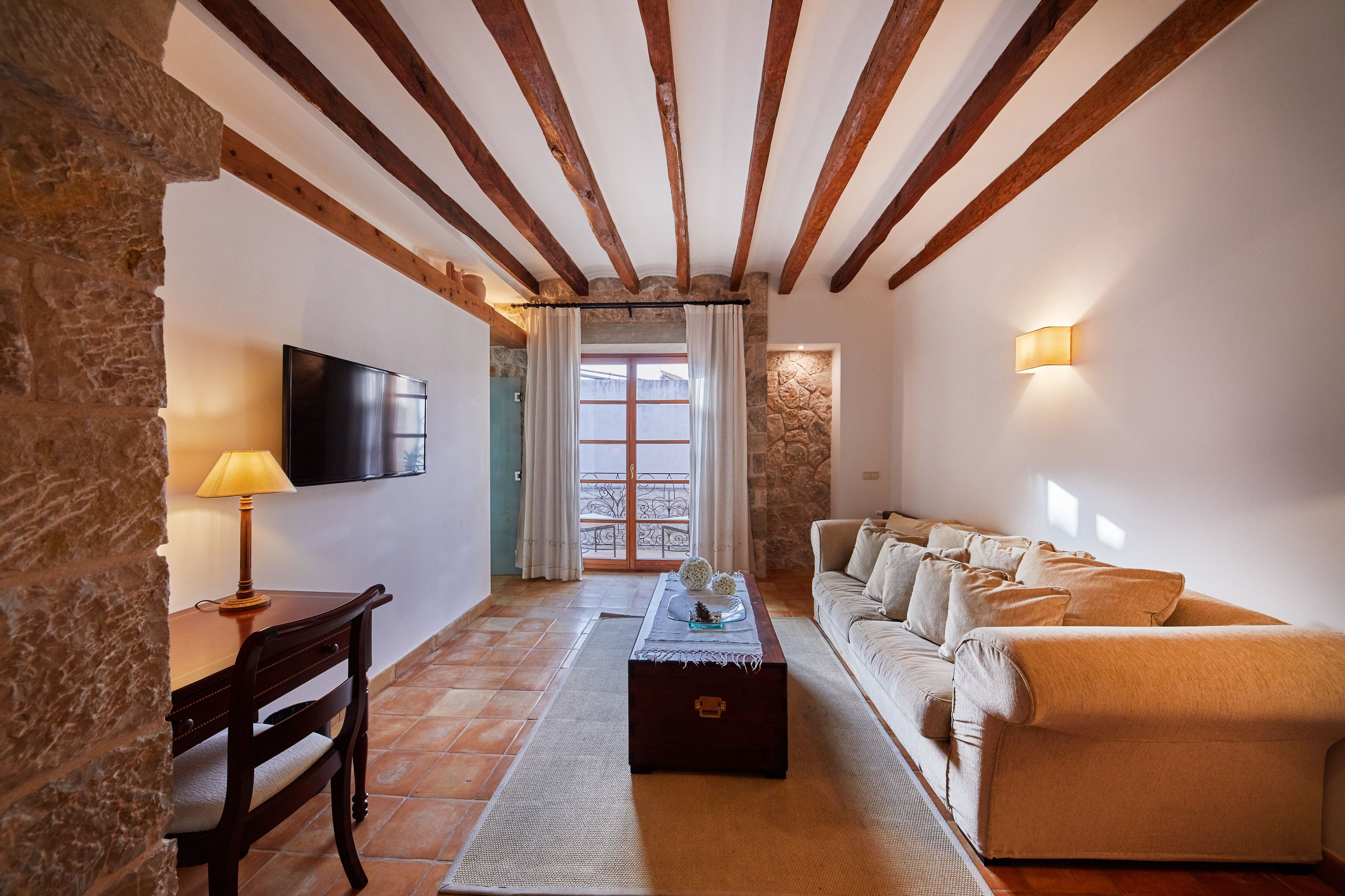 Uma sala de estar com teto de madeira, parede de pedra, televisão de tela plana, sofá, mesa de centro e luminária.