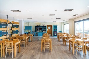Um café amplo com mesas e cadeiras de madeira, um balcão e grandes janelas.