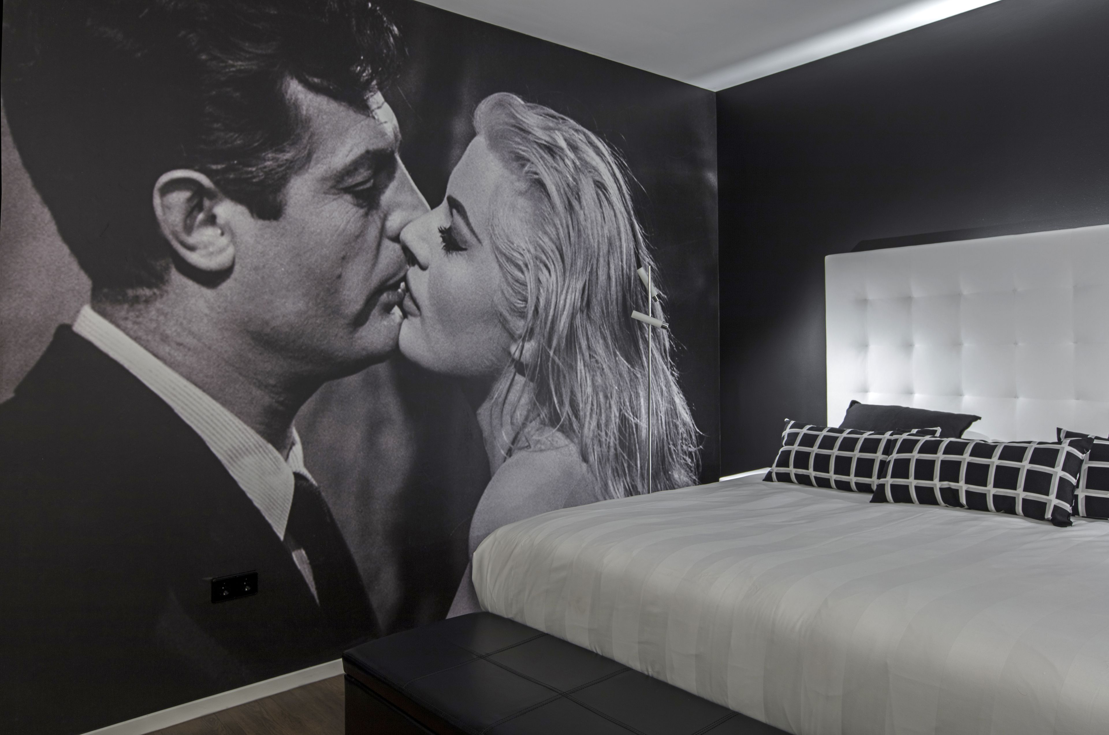 Quarto com uma cama grande, cabeceira estofada e uma obra de arte na parede retratando um casal.
