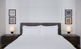 Quarto de hotel com uma cama grande, duas mesas de cabeceira e cartazes emoldurados nas paredes.