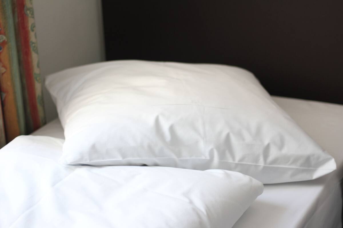 Cama bem arrumada com roupa de cama branca e um travesseiro.