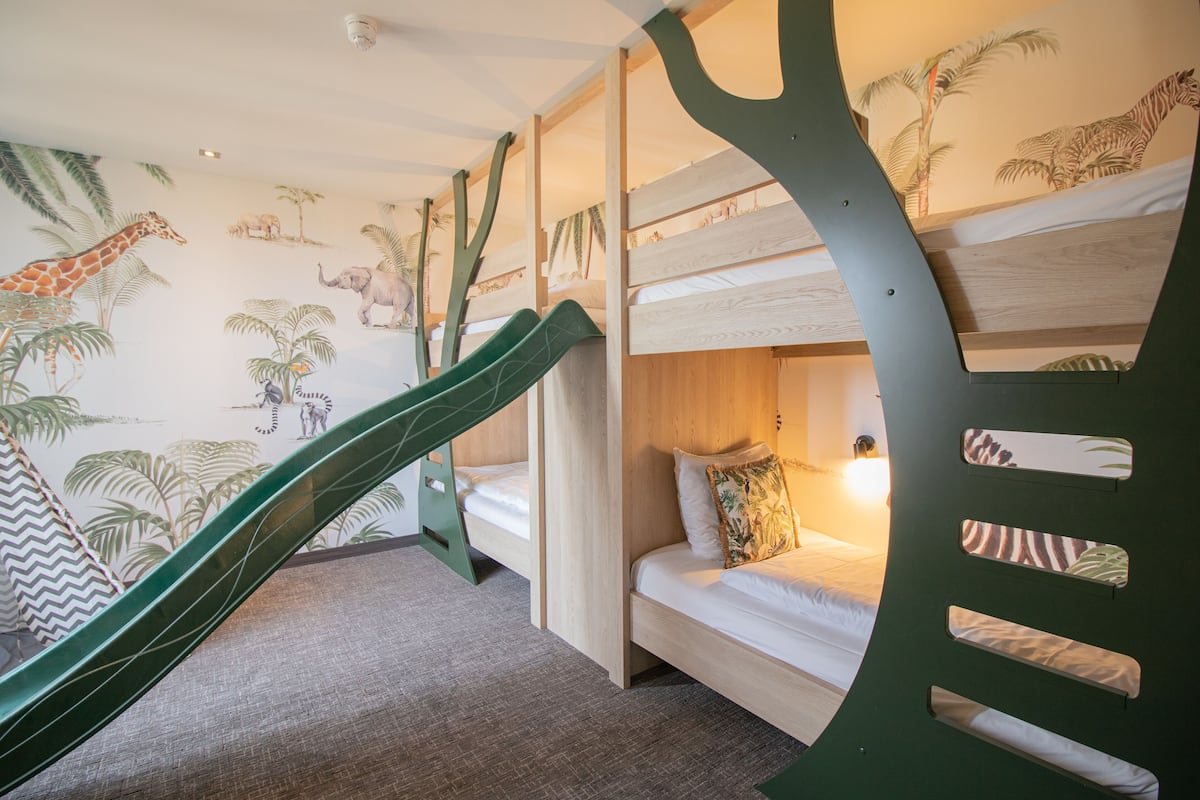 Quarto infantil com beliches, escorrega e um mural de animais.