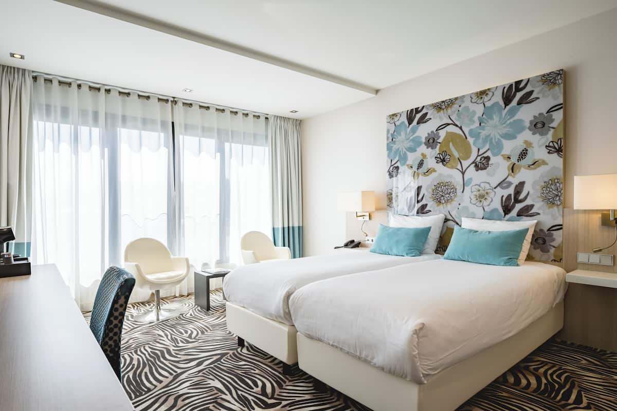 Quarto de hotel com uma cama grande, duas mesas de cabeceira, uma escrivaninha, uma cadeira e um tapete com padrão de zebra.