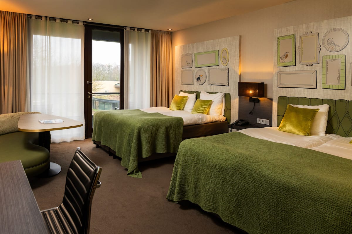 Quarto de hotel com duas camas, uma mesinha e uma cadeira.