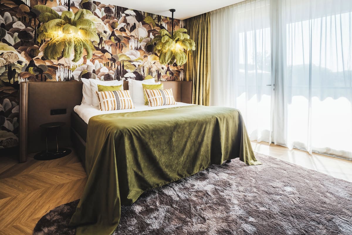 Quarto moderno com uma cama grande, um mural decorativo e uma janela ampla com cortinas leves.