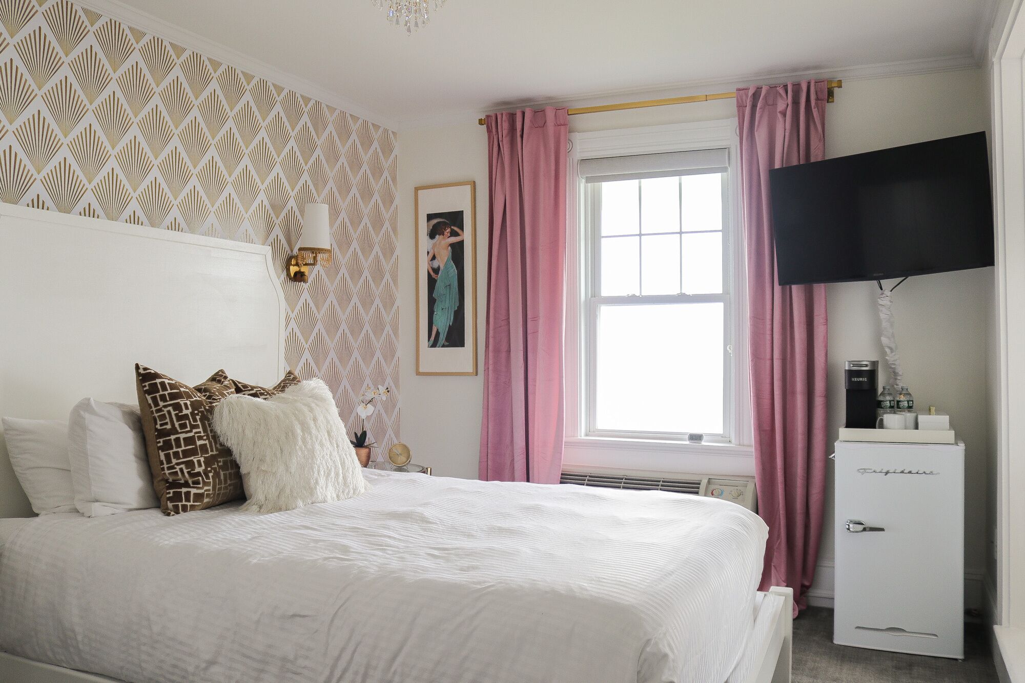 Quarto com cama, televisão, frigobar e janela com cortinas cor-de-rosa.
