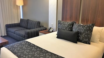 Quarto de hotel com uma cama, um sofá, uma mesa de cabeceira com um telefone e uma luminária.