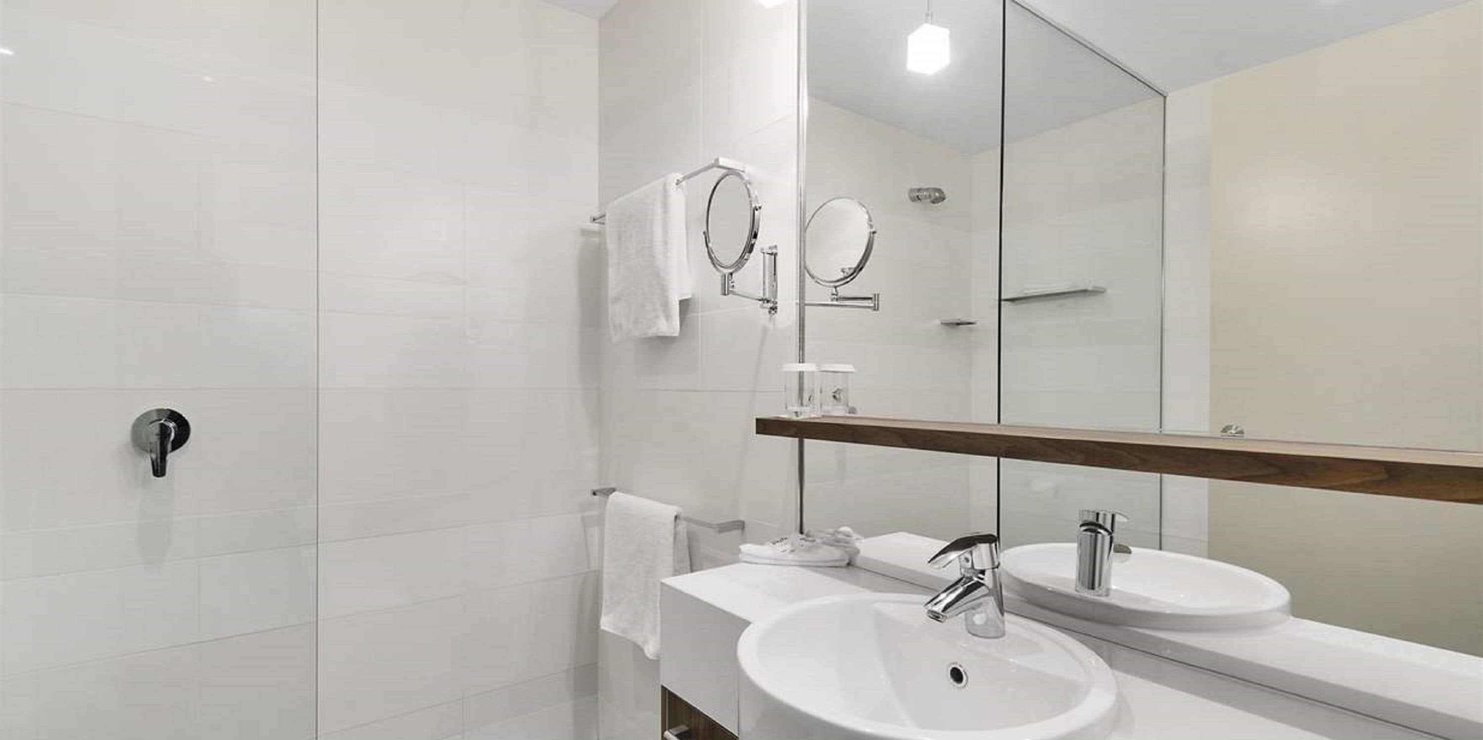 Uma casa de banho moderna com duas lavatórios, um espelho grande e cabine de duche em vidro.