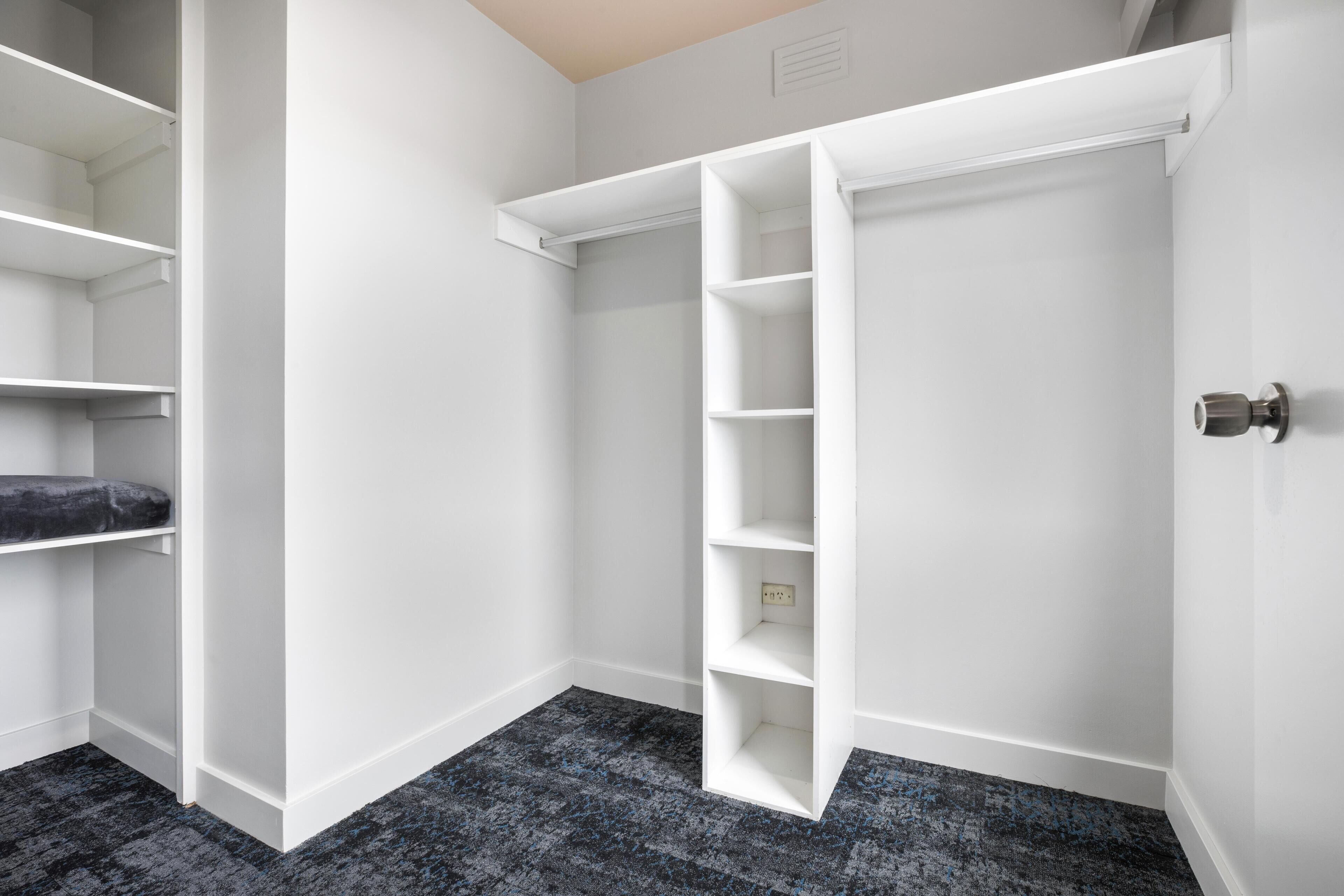 Um quarto com um armário branco, um tapete cinza e uma porta branca.