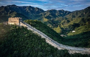 Trecho da Grande Muralha da China com uma torre de vigia, rodeado por montanhas verdejantes.