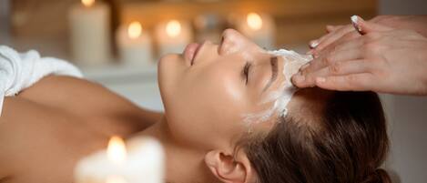 Uma pessoa recebendo tratamento facial com velas ao fundo.