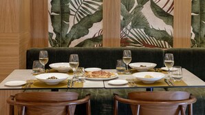 Mesa de jantar posta com pratos, copos e talheres, uma pizza e um sofá ao fundo.