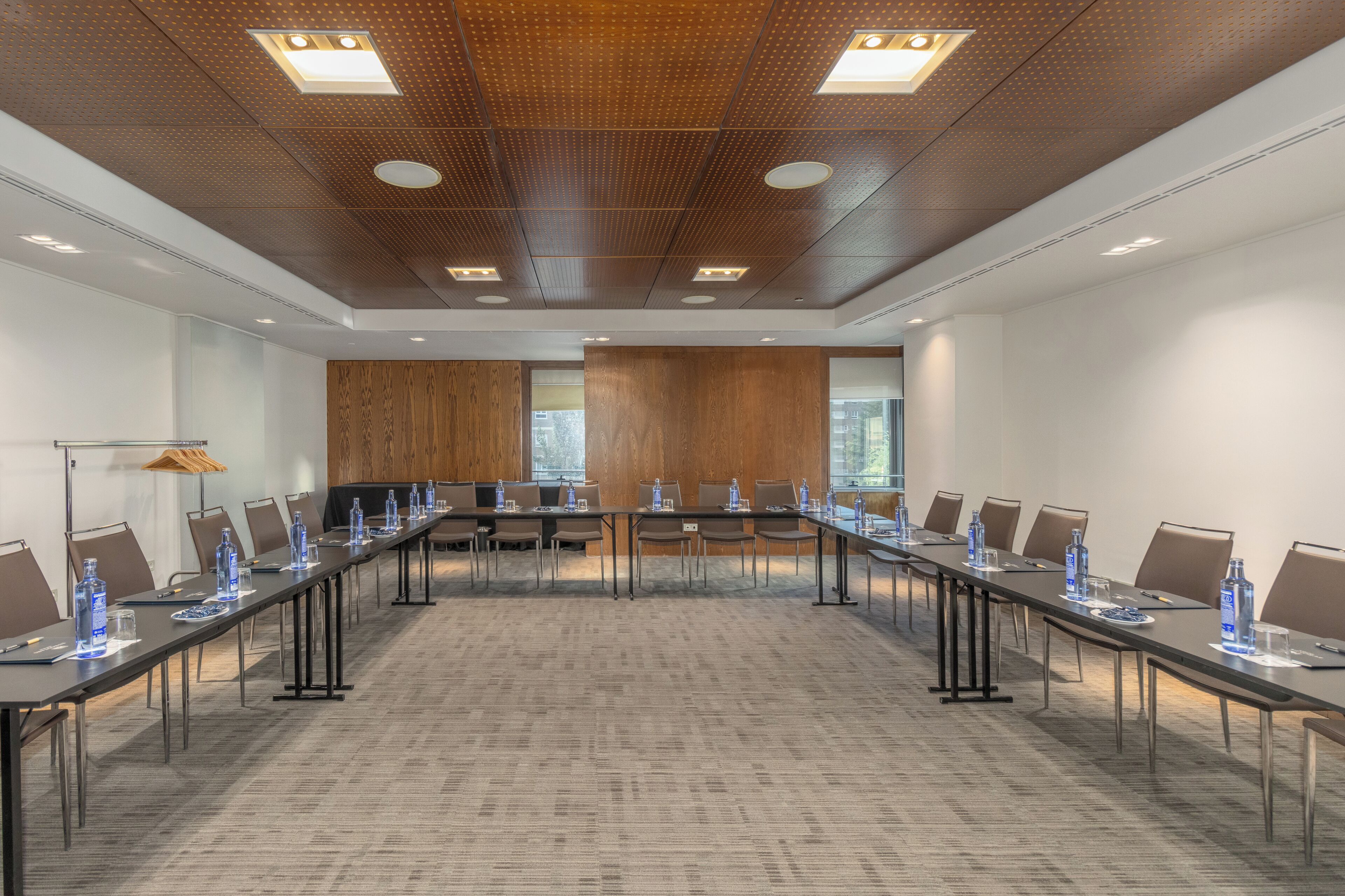 Sala de conferências com uma mesa comprida, cadeiras, garrafas de água e um painel de parede de madeira.