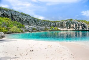 Uma praia com águas turquesa cristalinas, areia branca e falésias rochosas com vegetação.