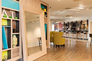Um interior moderno com piso de madeira, área de bar com banquetas e espaço de estar com uma poltrona amarela.