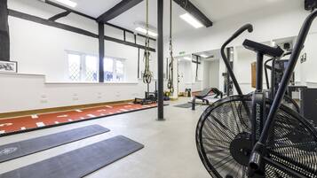 Academia com equipamentos de ginástica, tapetes e um grande ventilador.