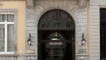 Uma entrada de edifício com arco de pedra, duas janelas com cortinas e uma varanda com grades.