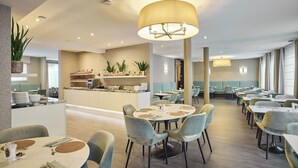 Uma área de jantar moderna com mesas redondas, cadeiras e uma ilha central com cozinha.