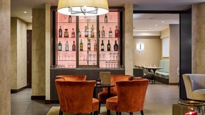 Uma área de bar com balcão de vidro exibindo garrafas de bebidas, uma mesa redonda com cadeiras e um espaço de estar com sofás.